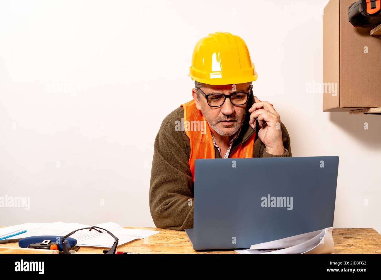 Contractor talking on cell phone while checking laptop in work office ...