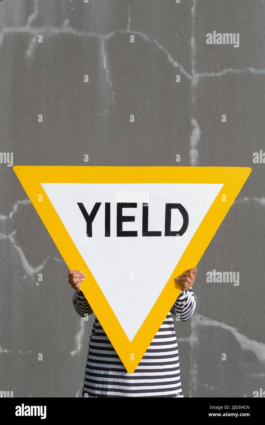 Person holds up big yield road sign. Bold yellow against cracked gray ...