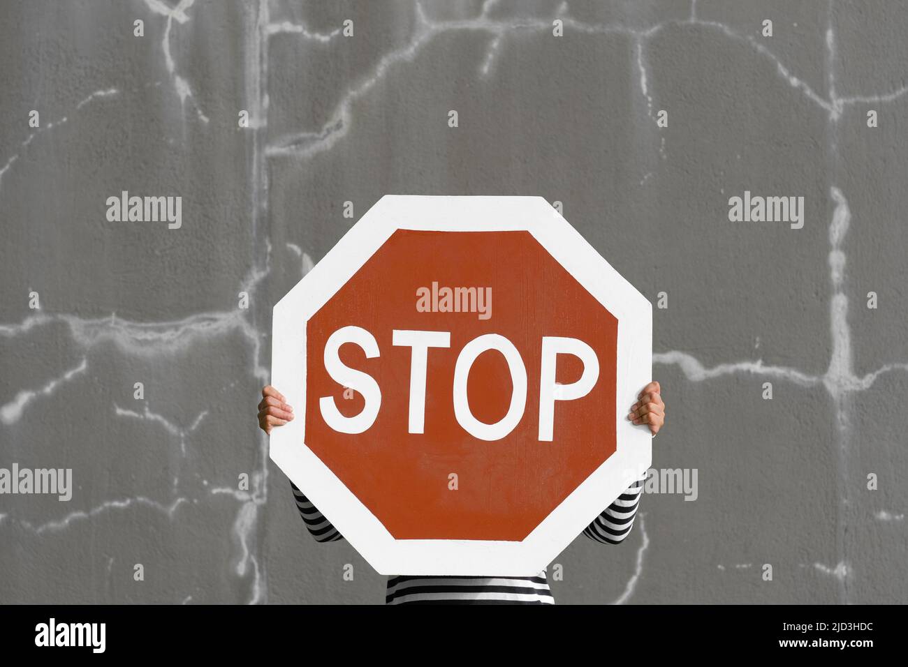 Person carries large stop road sign. Bold red against cracked gray wall ...
