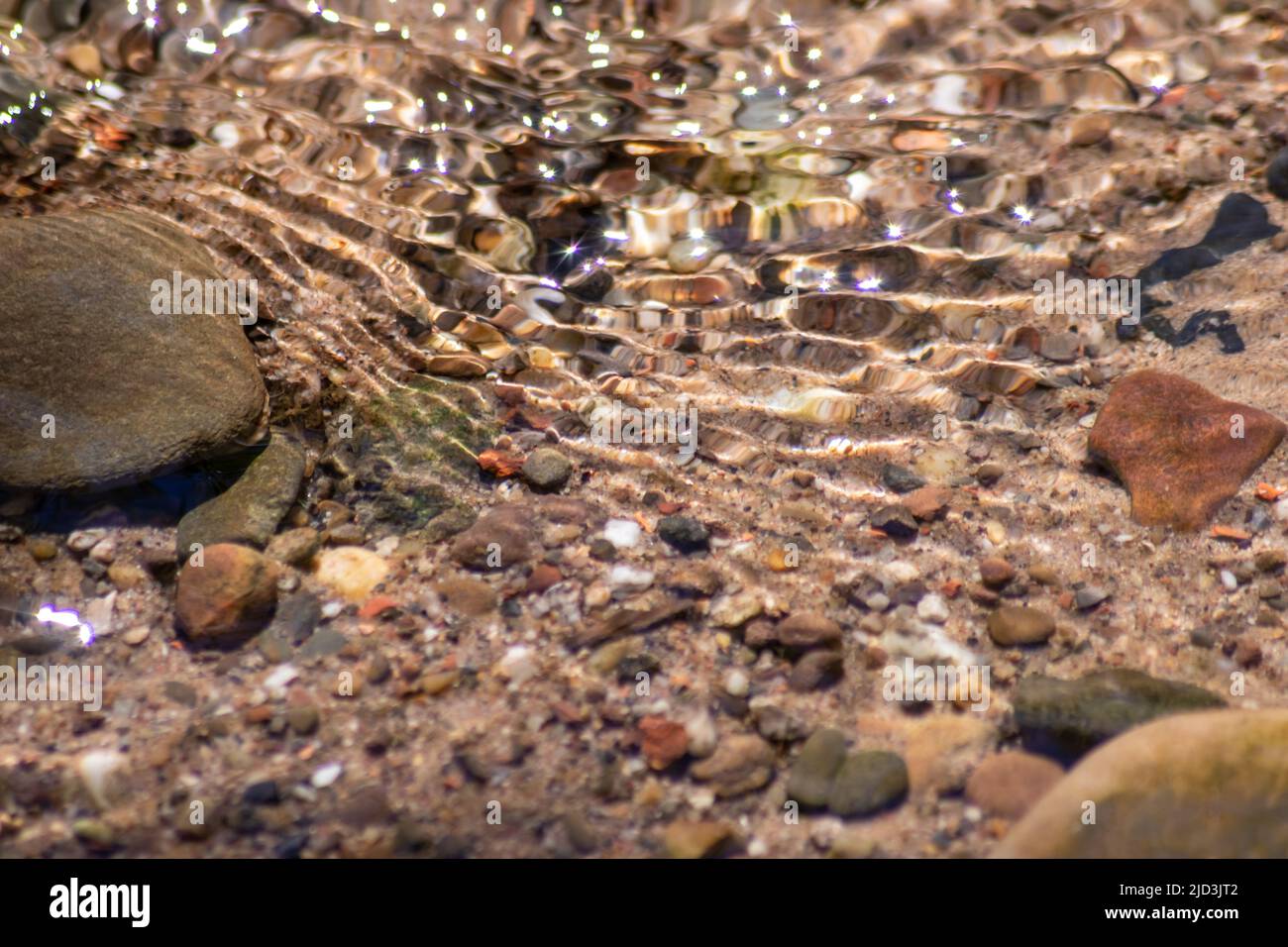 Stones in sparkling water with sunny reflections in water of a crystal ...