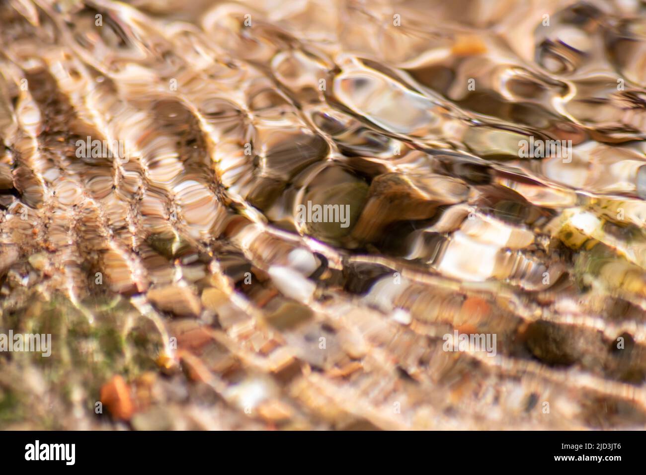 Stones in sparkling water with sunny reflections in water of a crystal ...