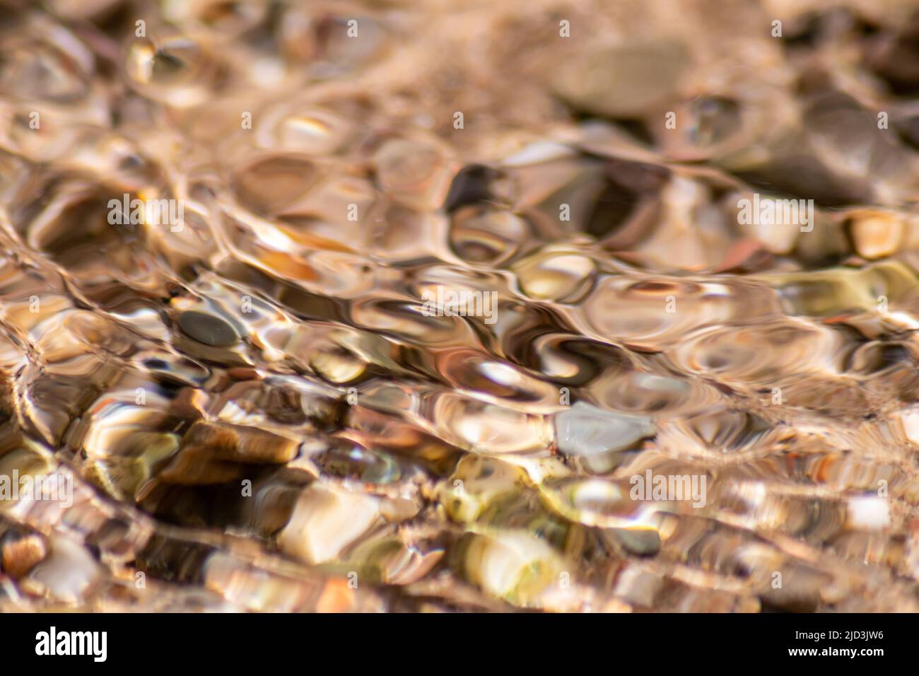 Stones in sparkling water with sunny reflections in water of a crystal ...