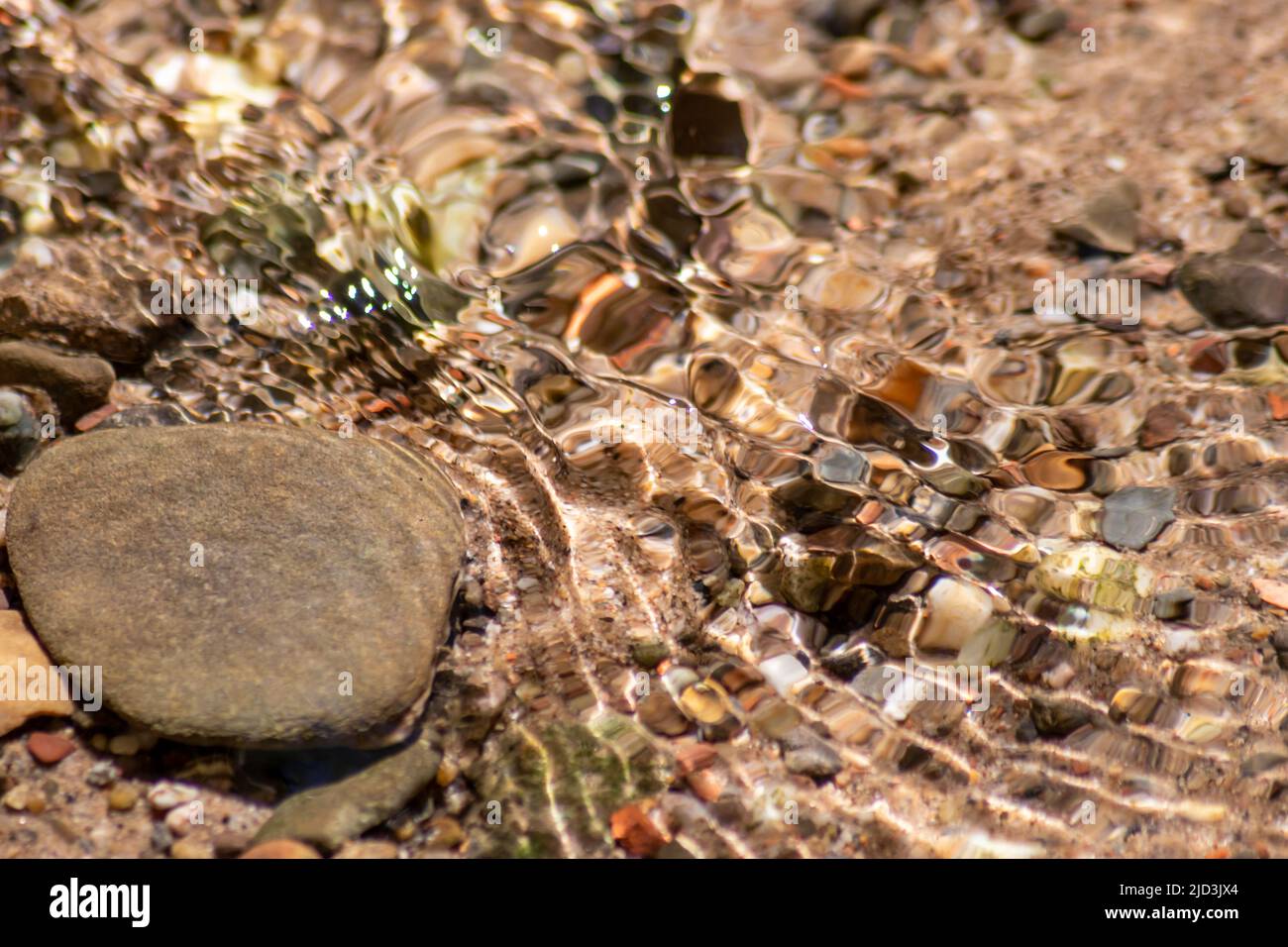 Stones in sparkling water with sunny reflections in water of a crystal ...