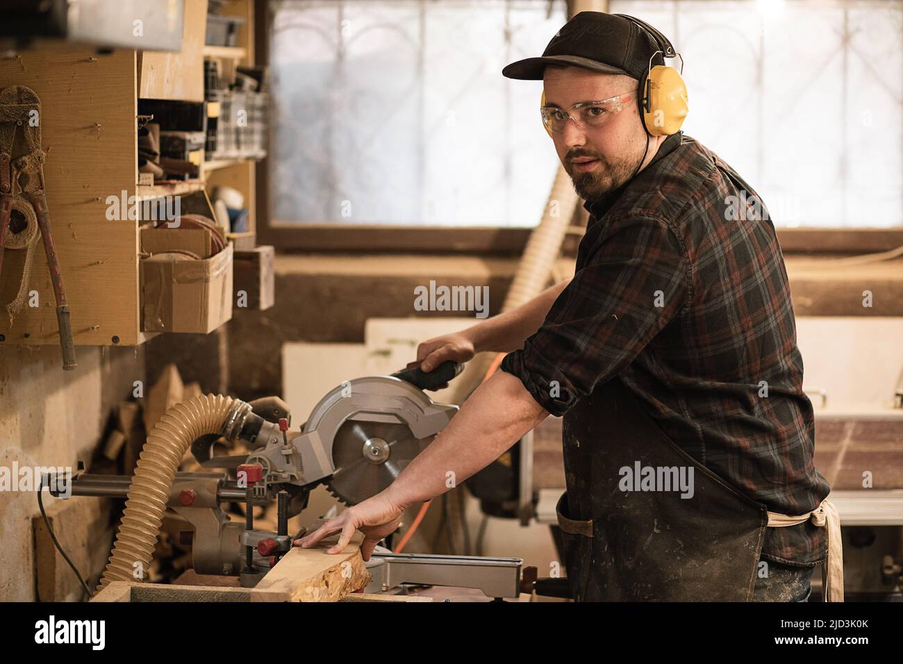 Carpenter worker in protective apron and headphones use grinder machine ...