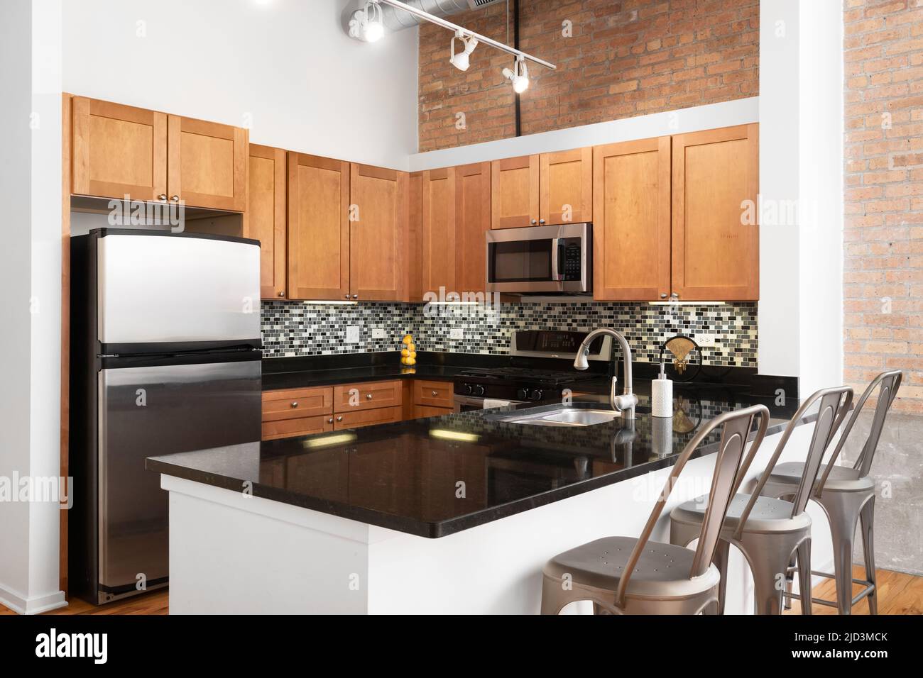 A loft kitchen with metal chairs sitting at a black granite countertop ...