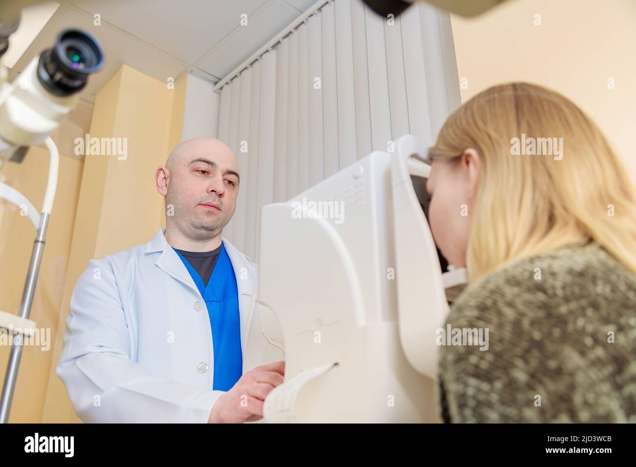 A male ophthalmologist checks the eyesight of a young girl using a ...