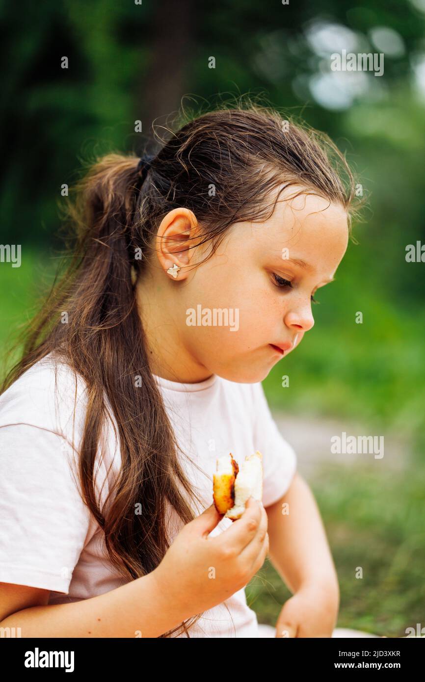 Side view of little thoughtful girl wth dark hair holding sandwich ...