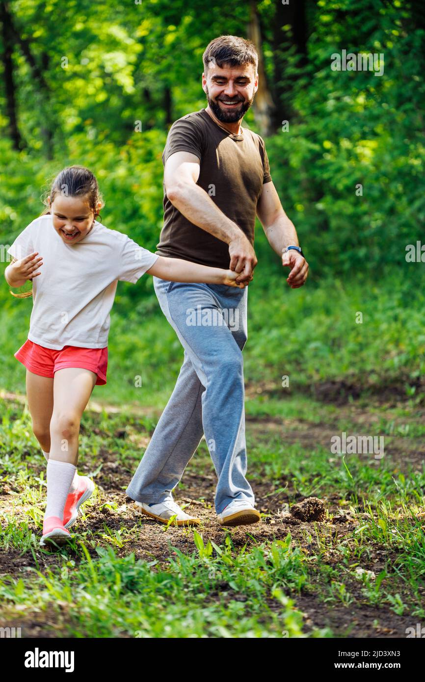 Portrait of family playing game of catch in park around trees. Little ...
