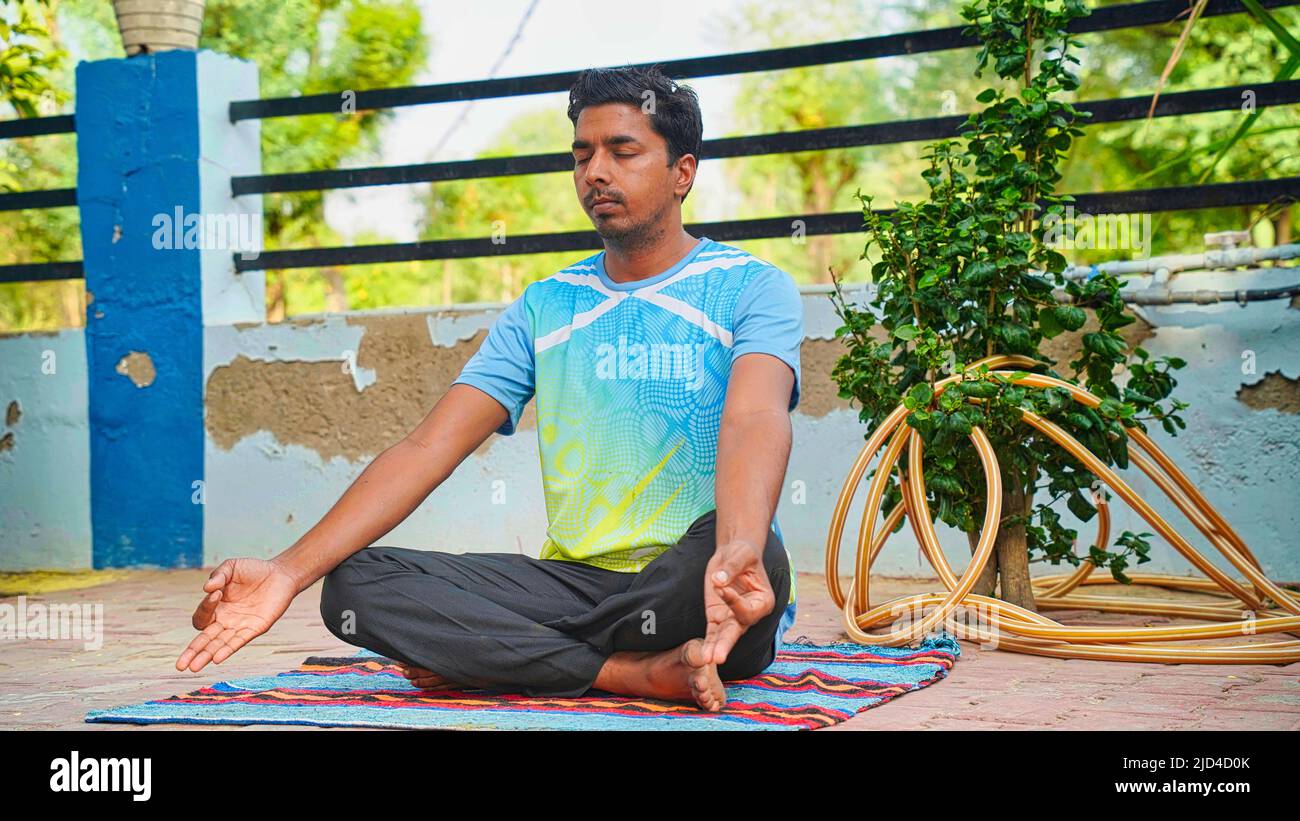 Attractive young Indian man sitting in yoga pose at home. Practicing ...