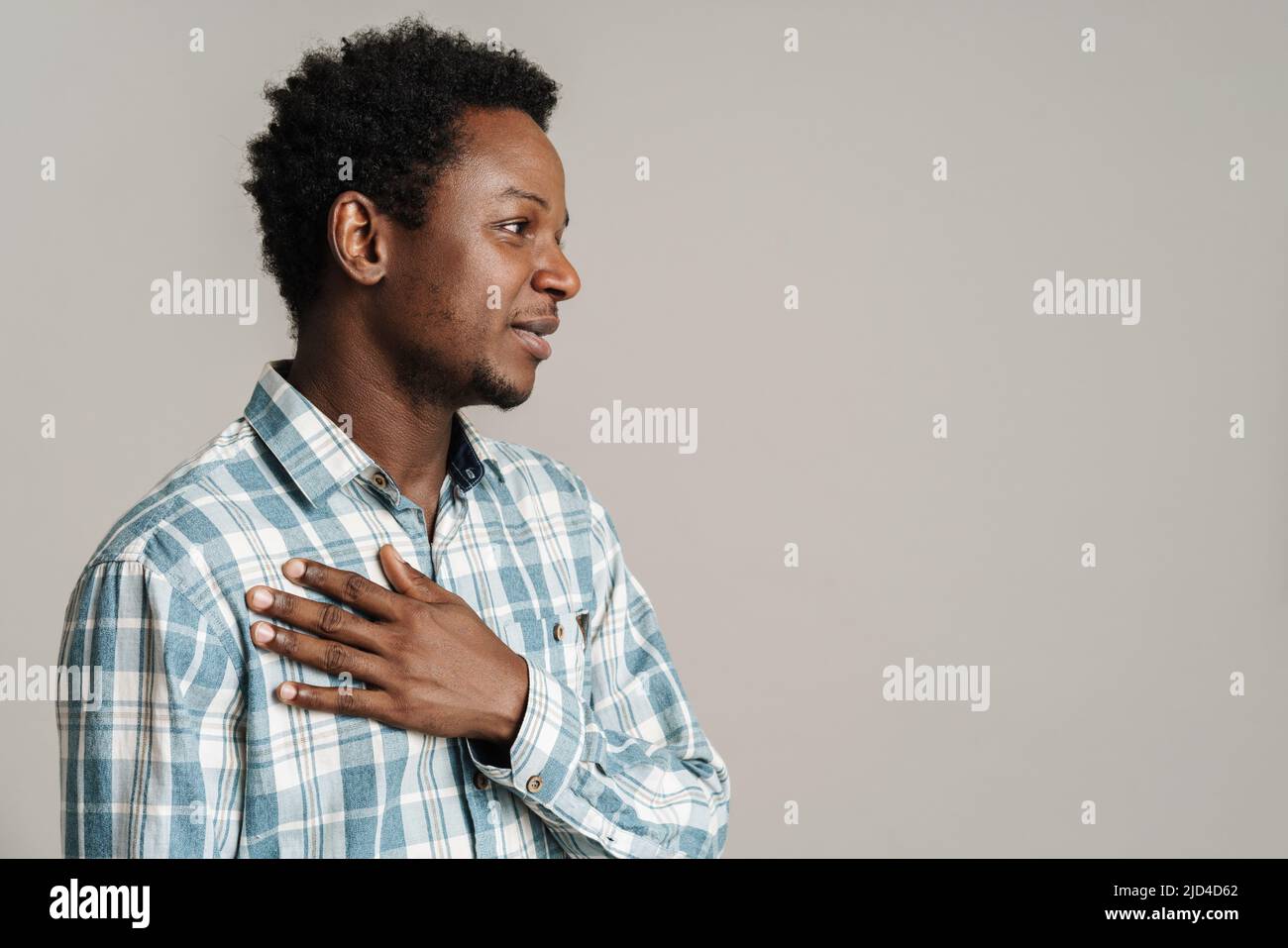 Black unshaven man holding hand on his chest while looking aside ...