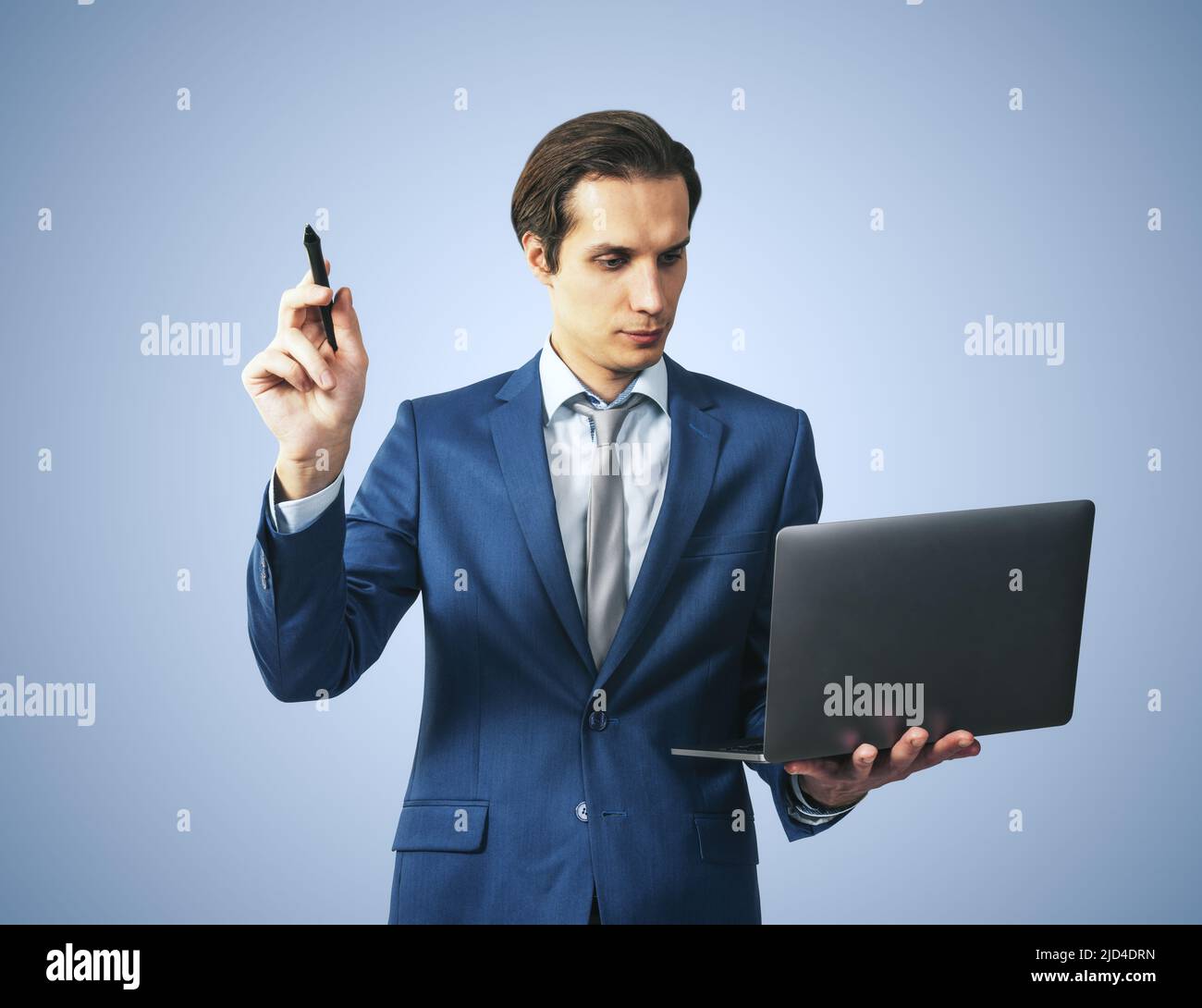Young man in blue suit goint to write with pen and laptop in hands ...