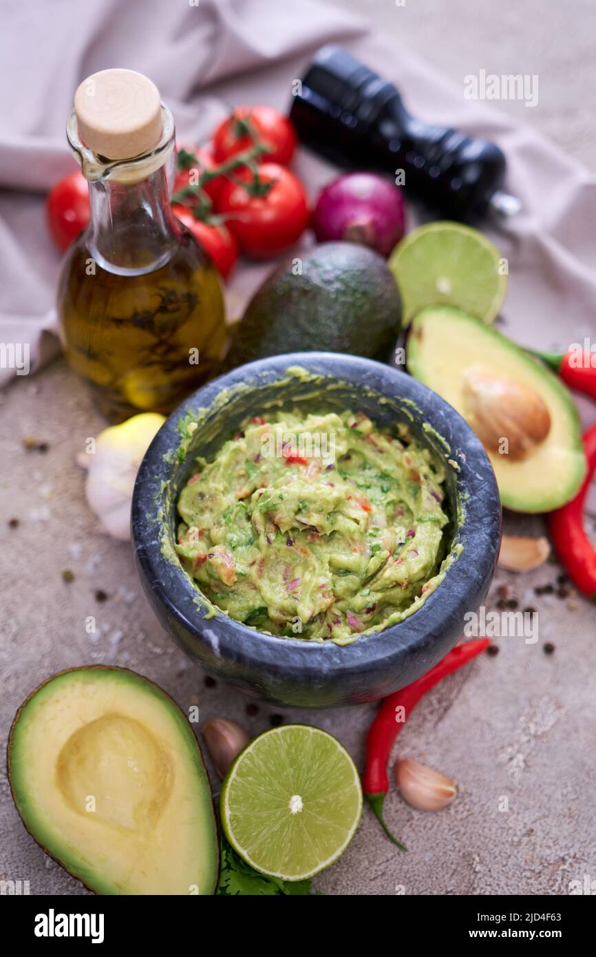 freshly made guacamole in marble mortar with ingredients on grey ...