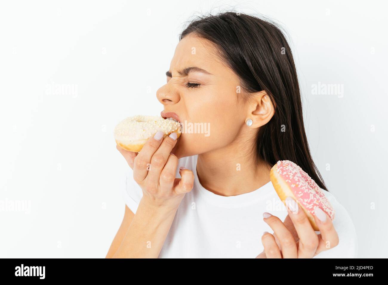 Hungry young woman bites greedily into sweet donut, enjoying the ...