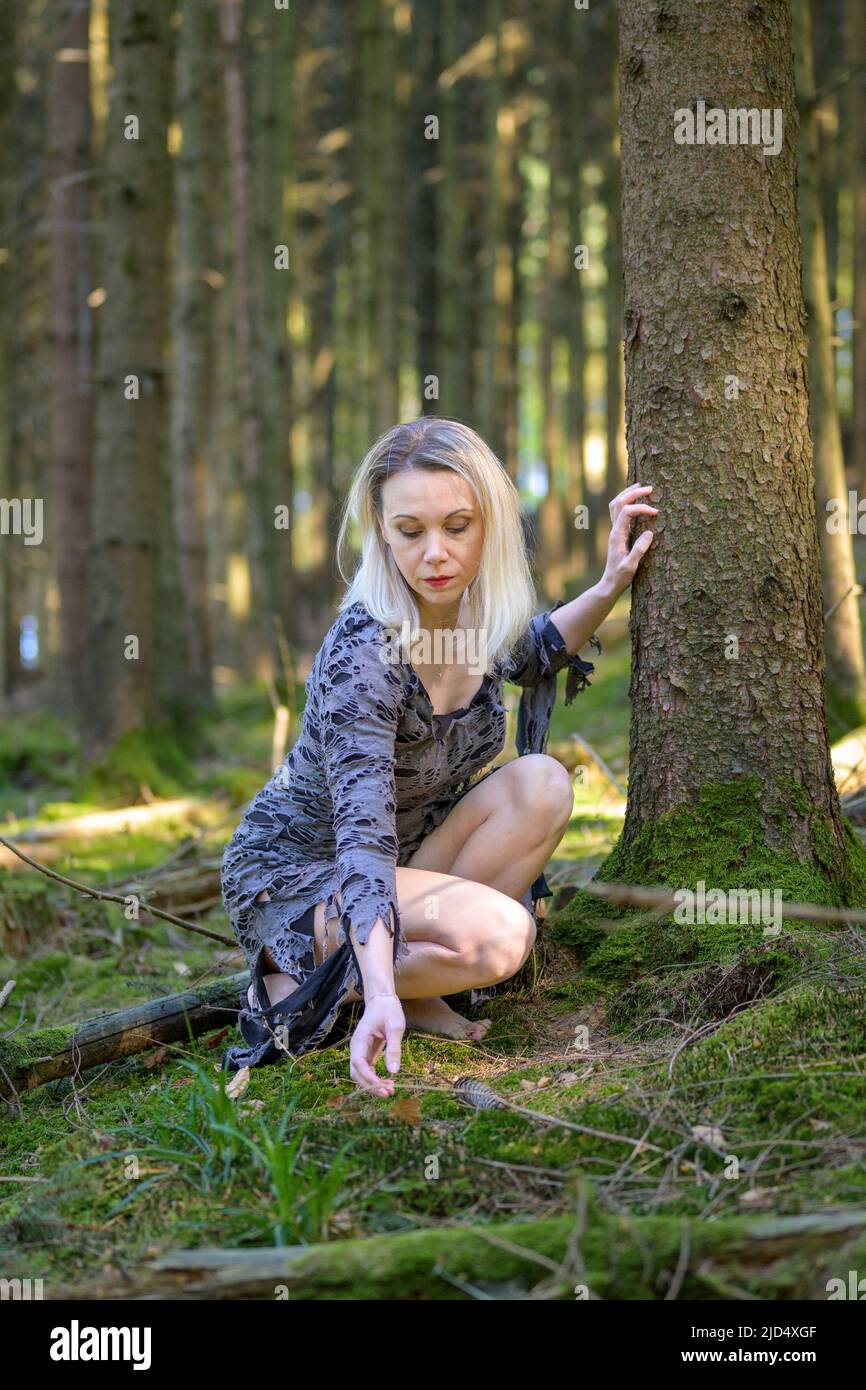 Elegant blond woman reaching down to a mossy forest floor as she poses ...