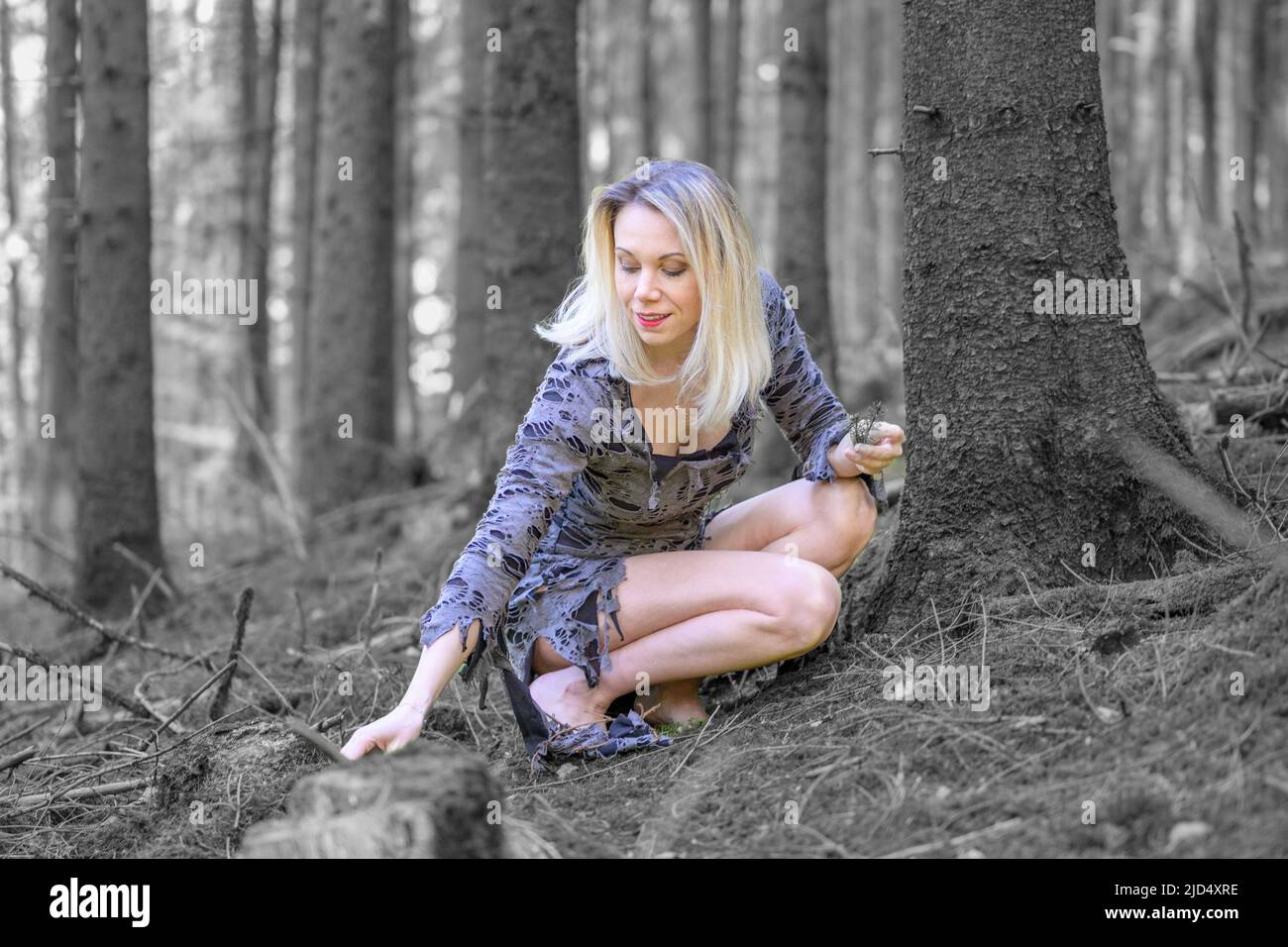 Carefree barefoot woman crouching on a forest floor in tattered dress ...