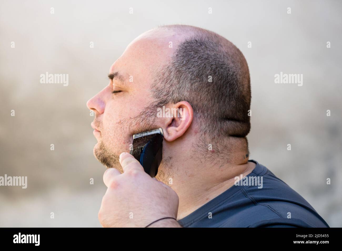 Male shaving or trimming his beard using a hair clipper or electric ...