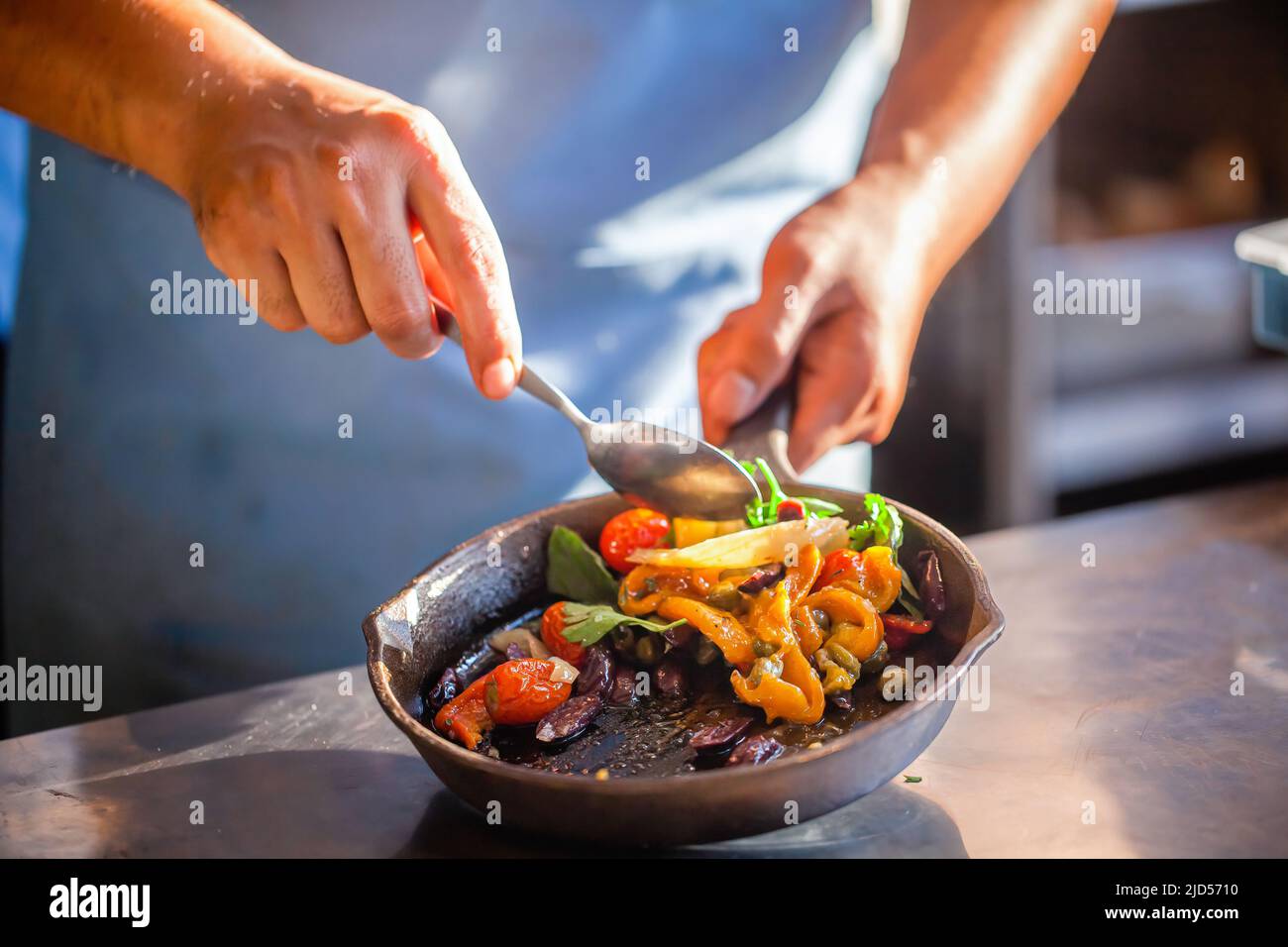 Gourmet chef in uniform preparing meal, stirs with spoon vegetable in ...