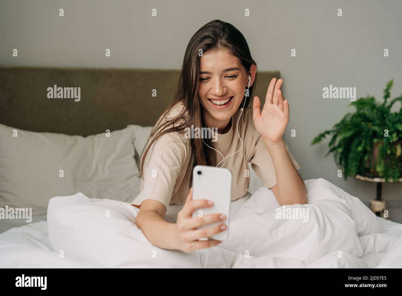 Woman sitting on bed after waking up and talking on video call using ...