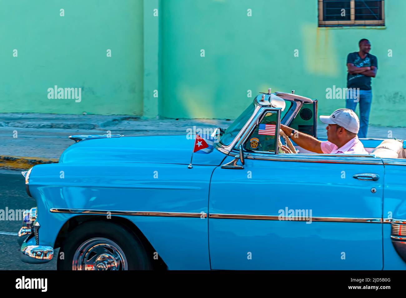 A light blue vintage car with small Cuban flag dries through the street ...