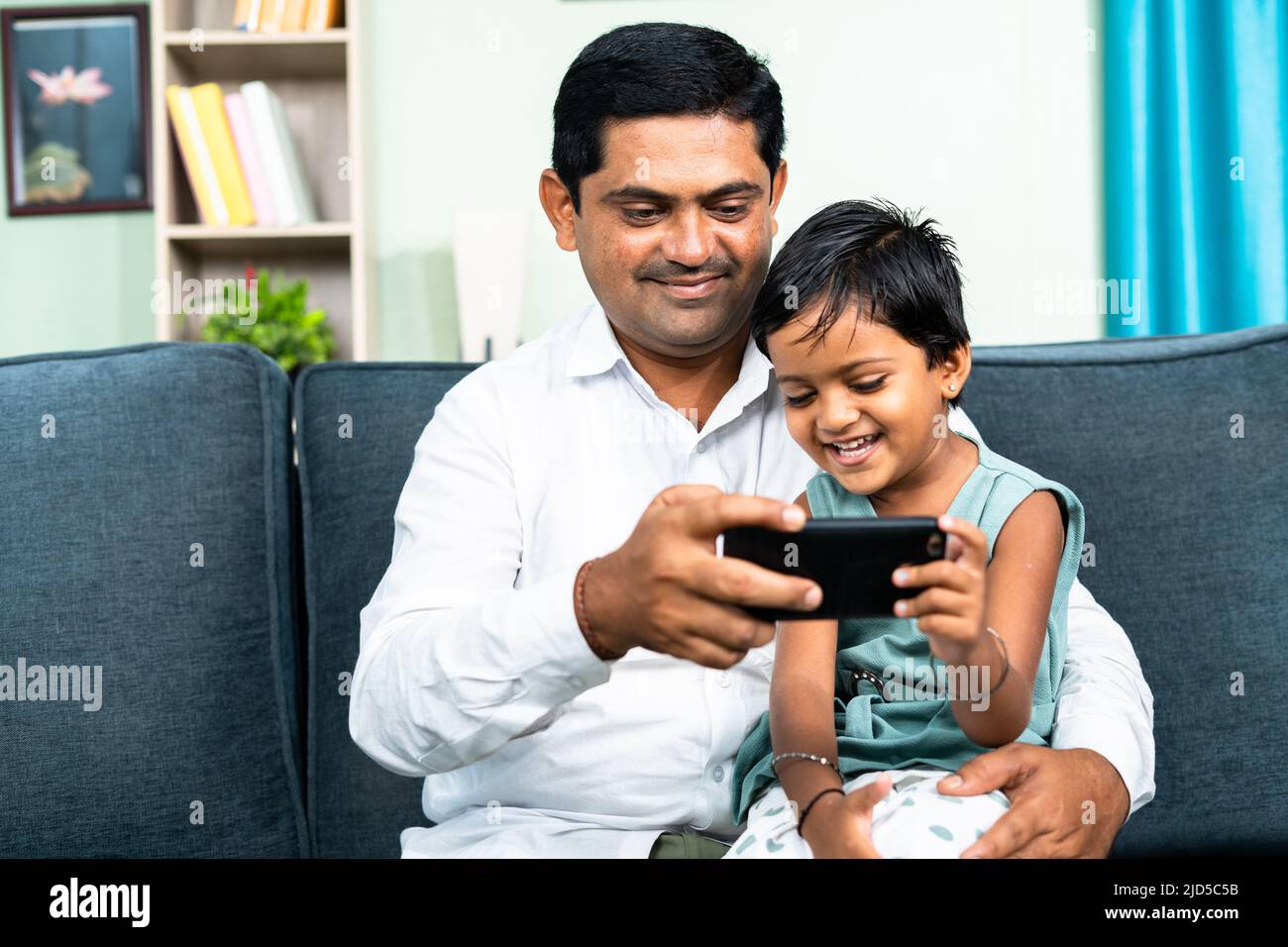 Happy smiling father and daughter looking camera while sitting on sofa ...