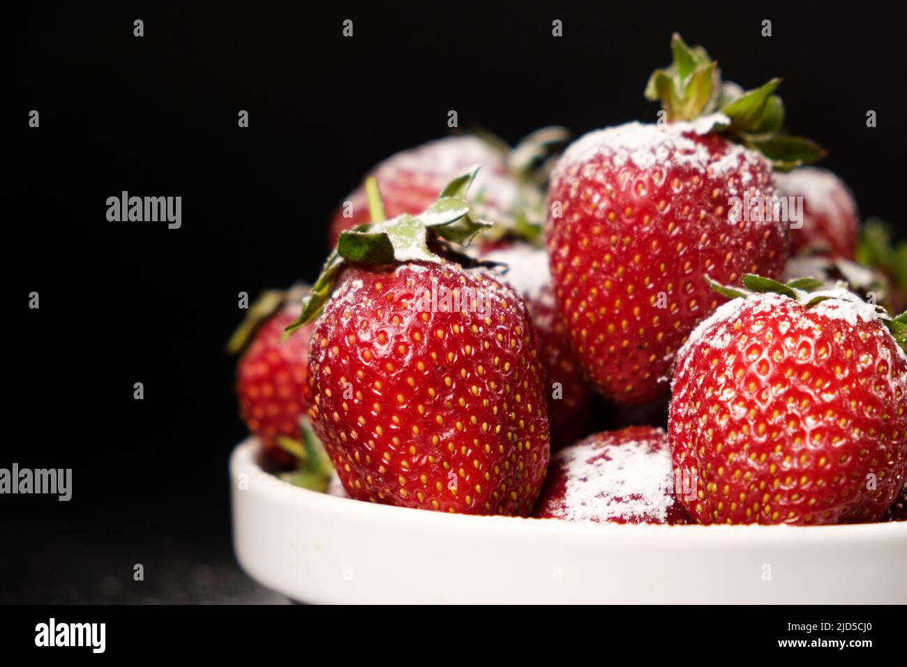 Strawberries in a plate with powdered sugar on a black background, side ... Strawberries in a plate with powdered sugar on a black background, side ...