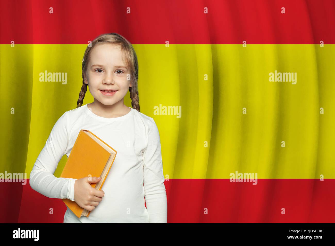 Adorable child girl with yellow book on flag of Spain background. Learn ...