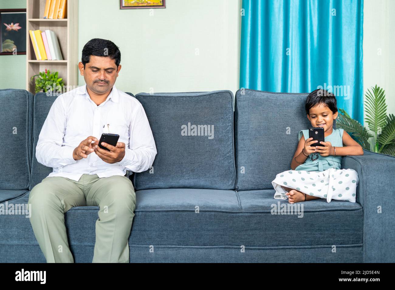 Father and daughter on sofa separately busy using mobile phone at home ...