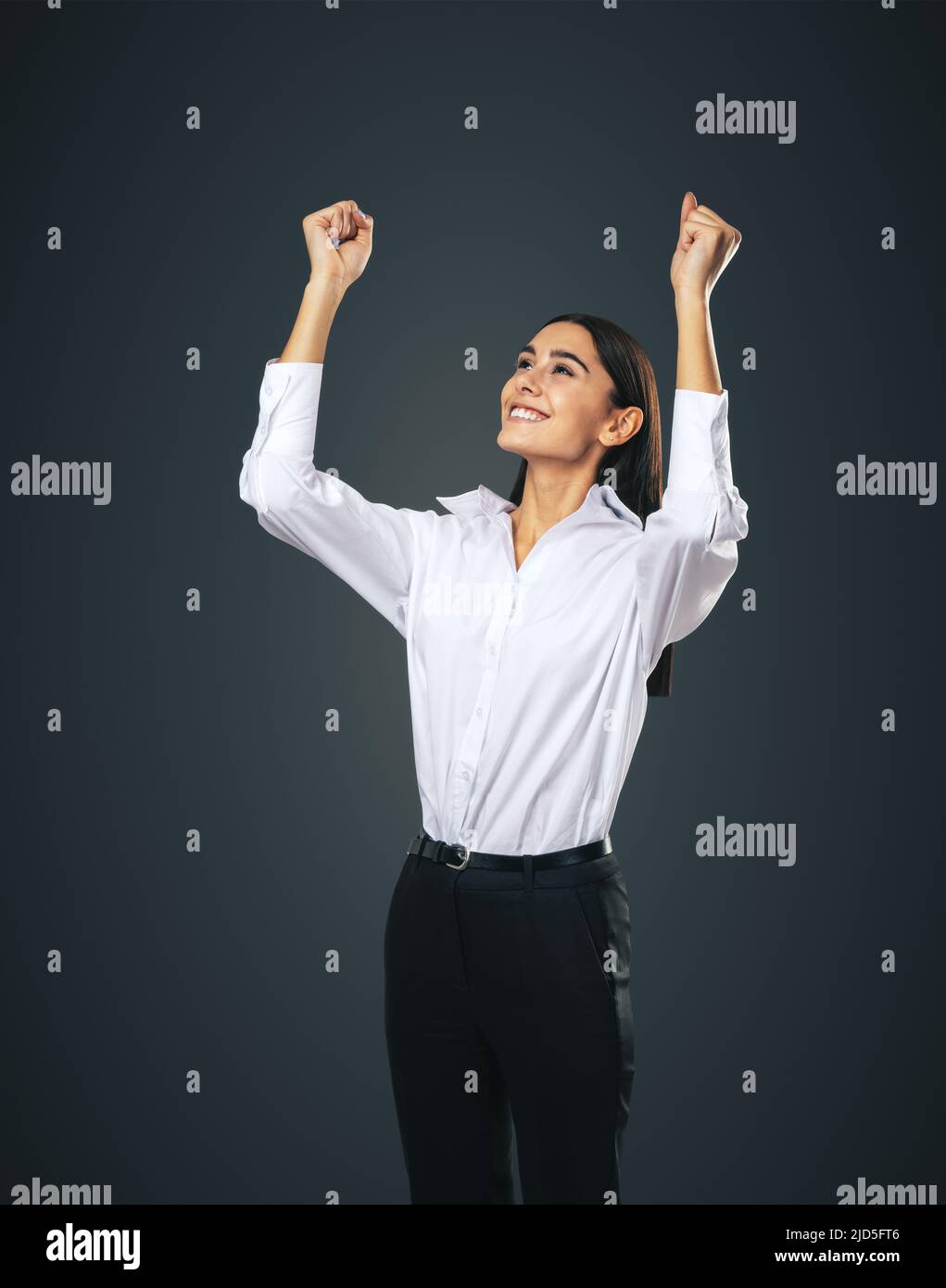 Joyful and satisfied woman in white shirt with raised hands showing her ...