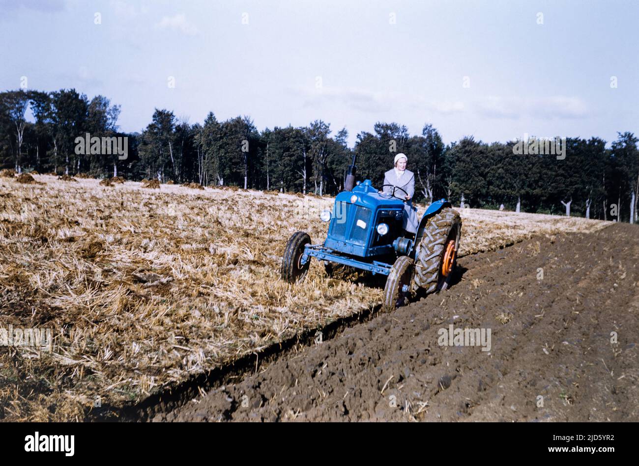Historical photo of a woman wearing a coat driving a tractor ploughing ...