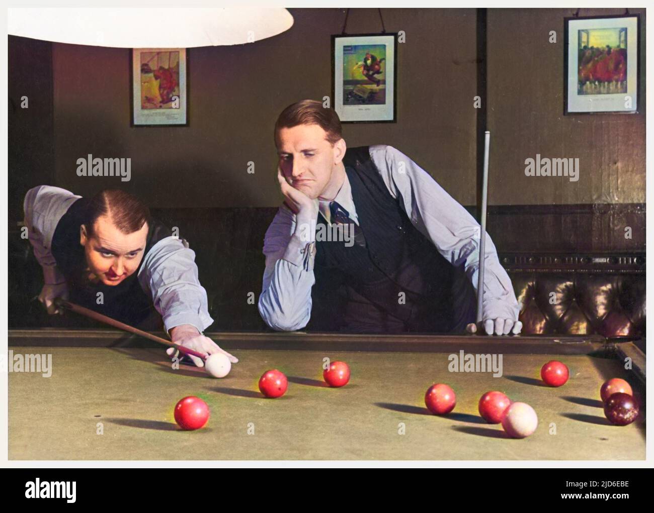 A snooker player prepares to play a shot as his partner looks on. Their ...