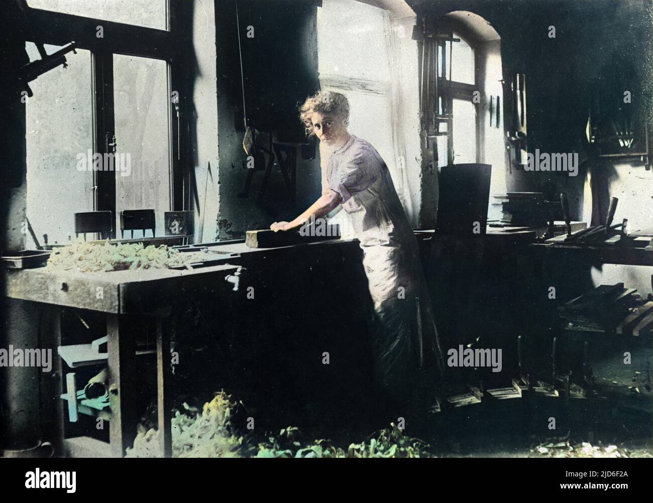 A German woman carpenter, planing wood in her workshop. Colourised ...
