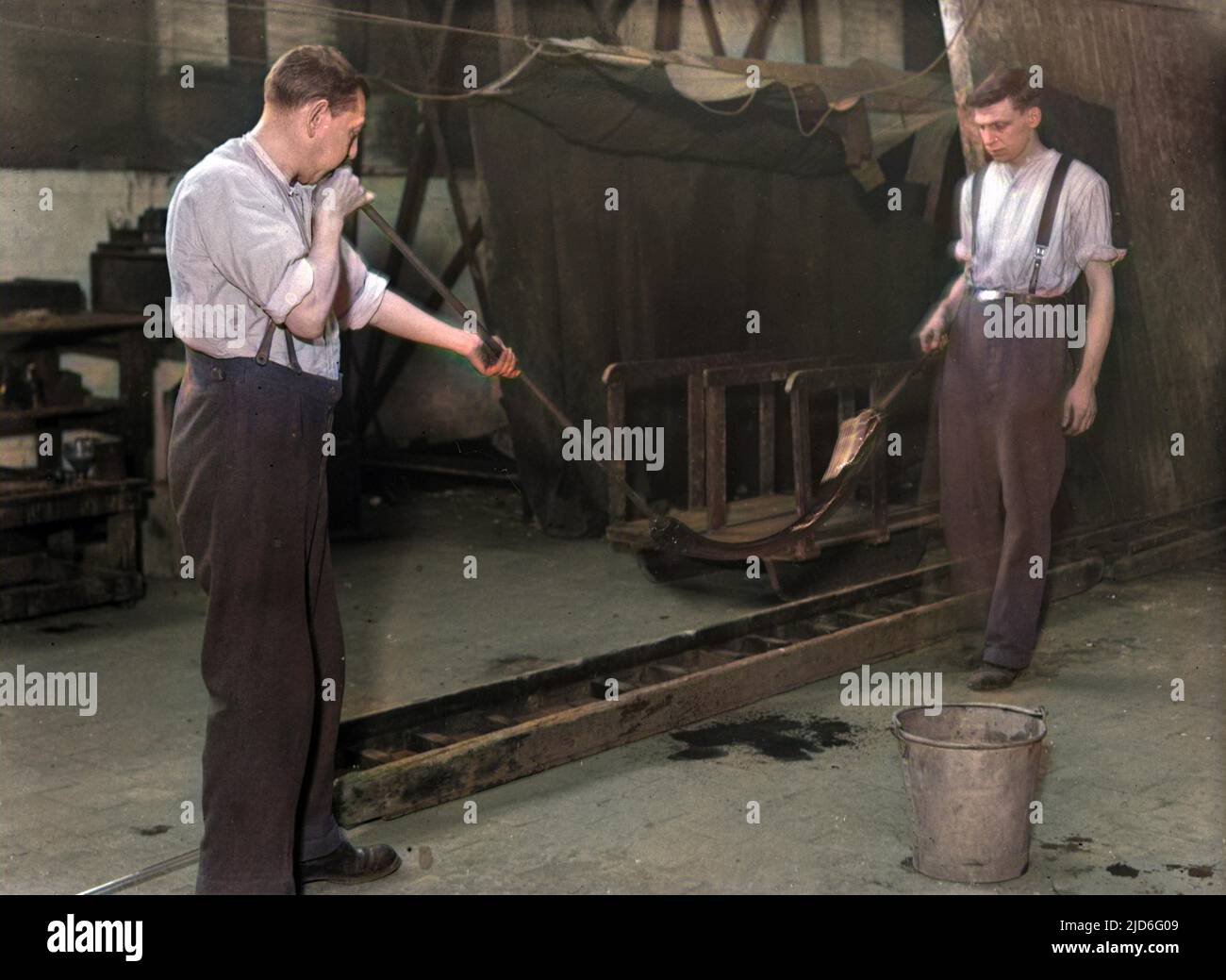 Glass making in a factory : Two men drawing out a glass rod. Colourised ...