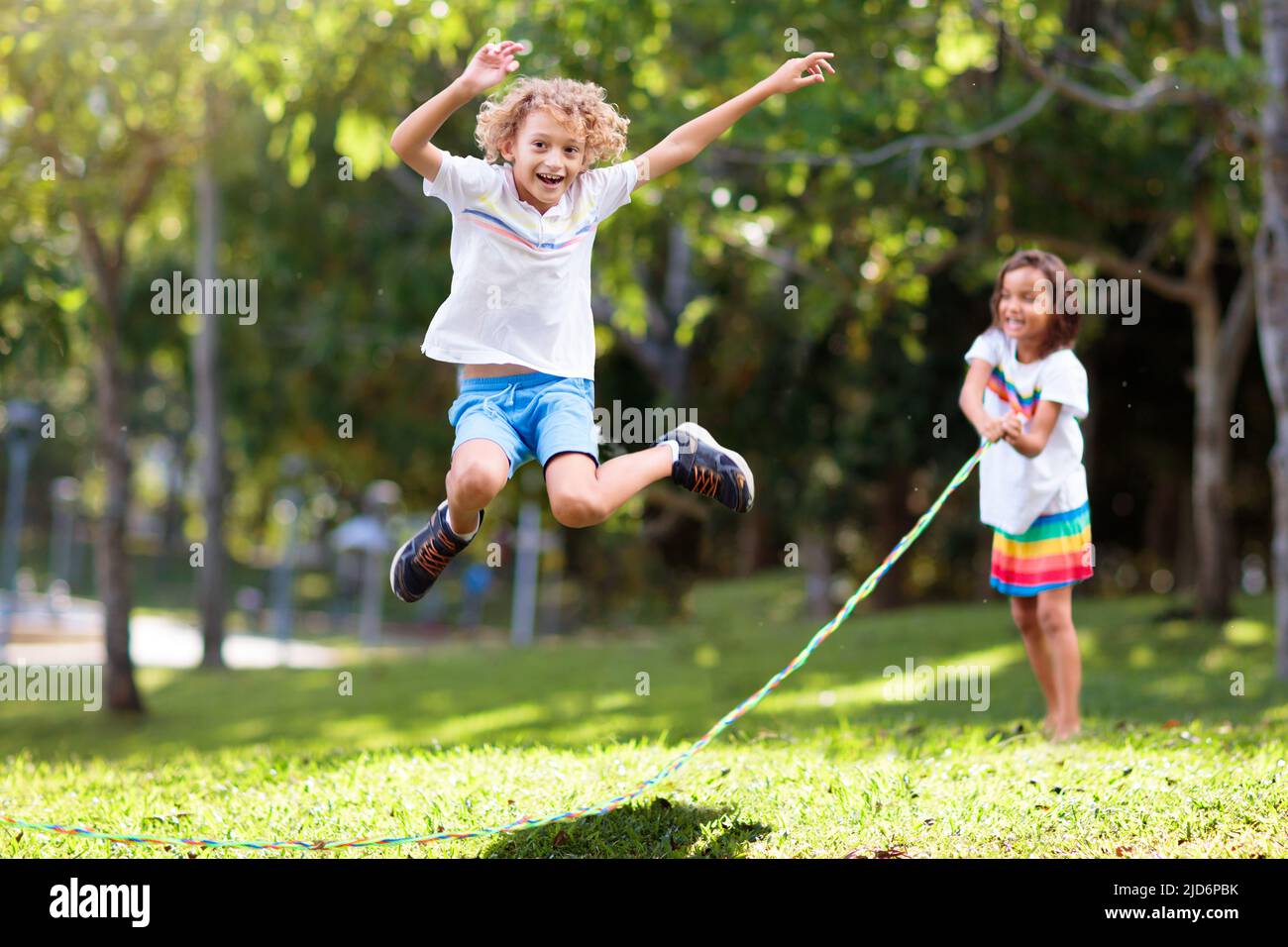 Happy kids play outdoor. Children skipping rope in sunny garden. Summer ...