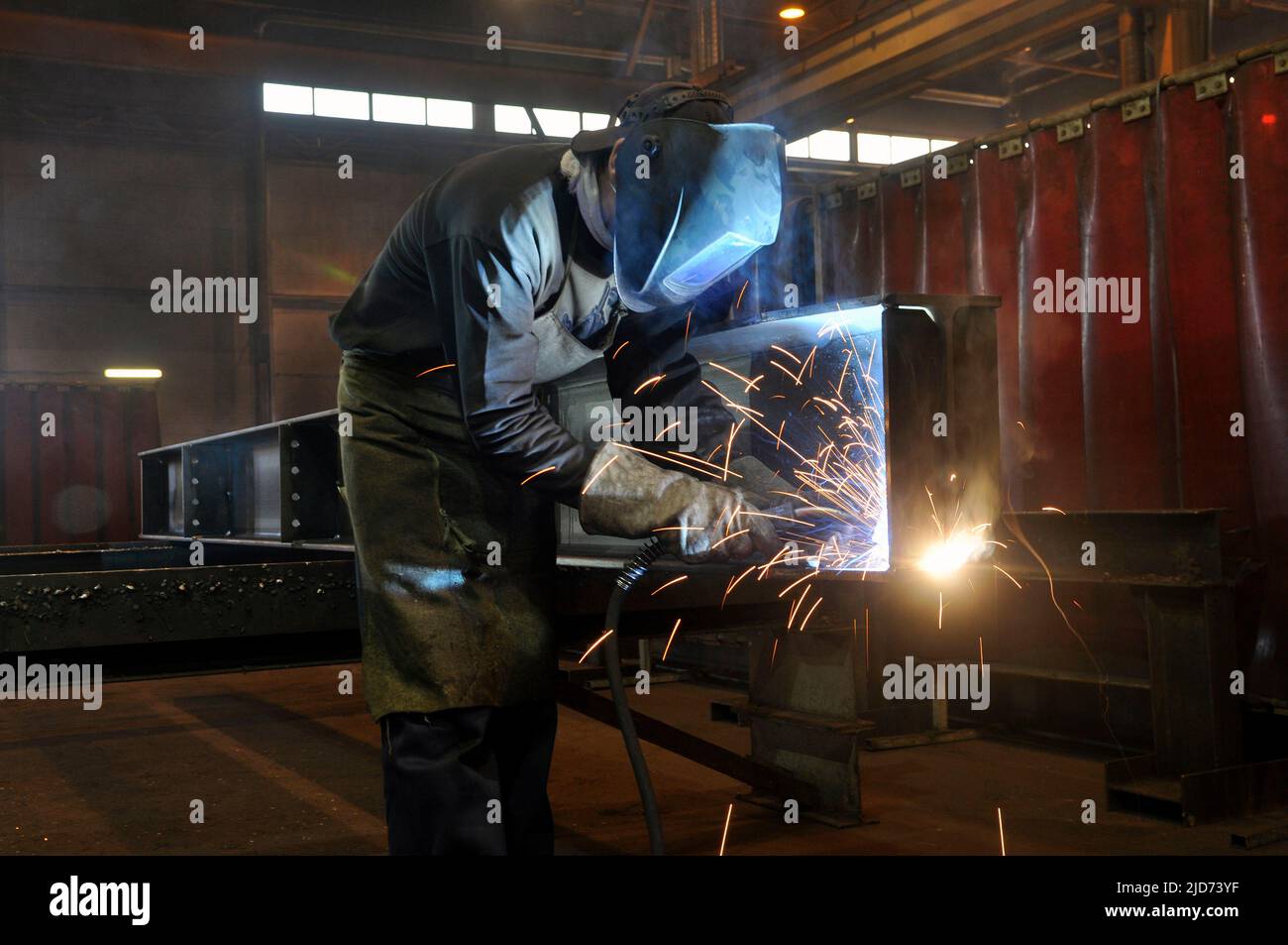 A welder in protective overalls and a welding mask welds metal ...