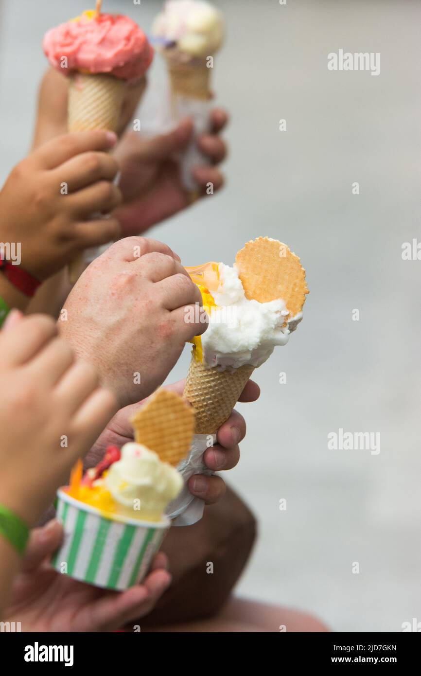 Family eating an ice cream sitting in the street, detail of the hands ...