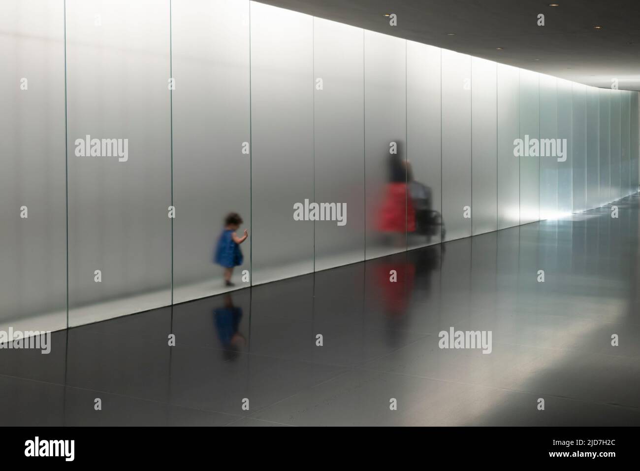 A young girl walks behind her mother behind a transparent walkway in ...
