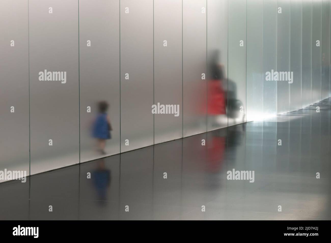 A young girl walks behind her mother behind a transparent walkway in ...