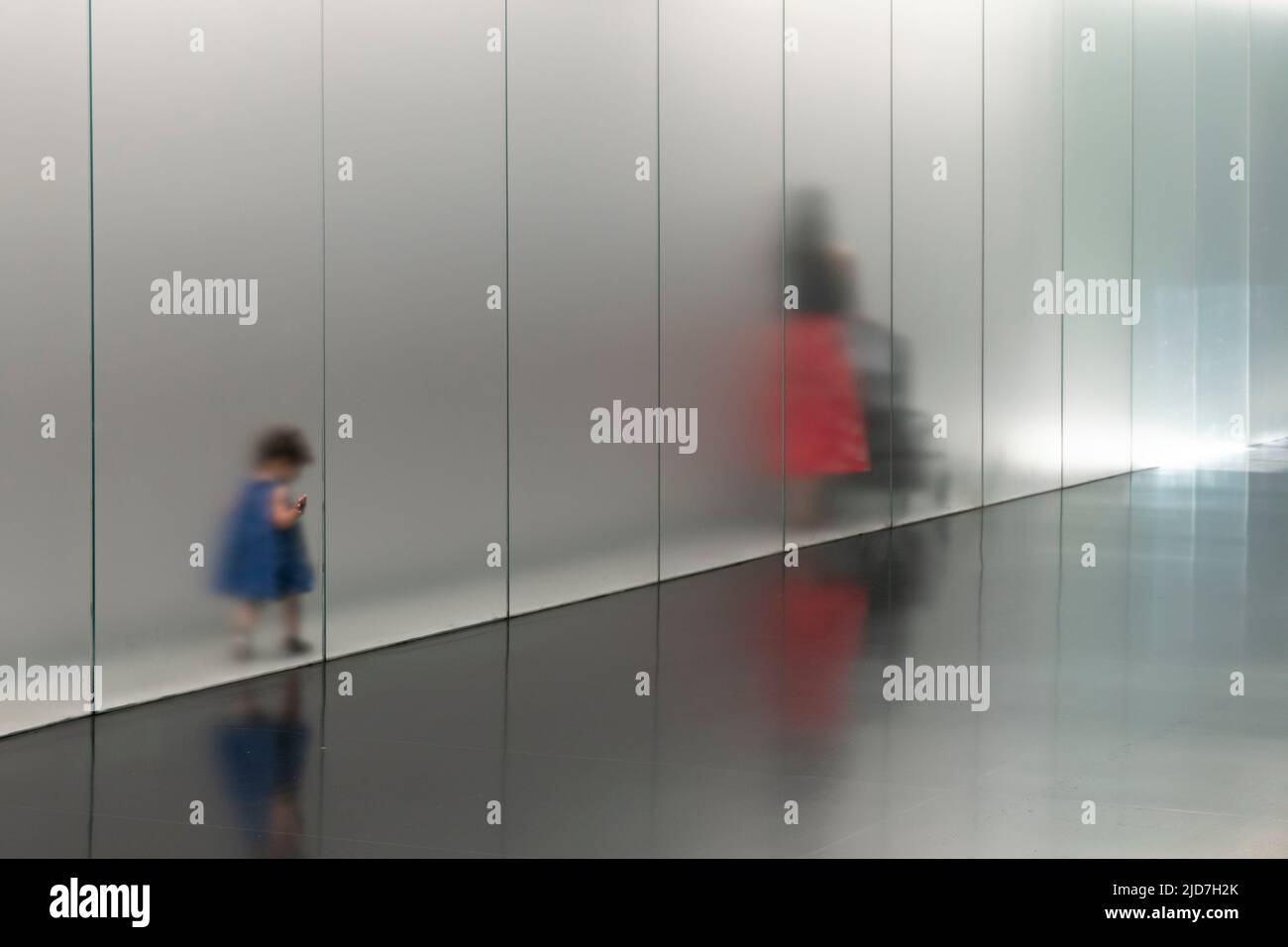 A young girl walks behind her mother behind a transparent walkway in ...