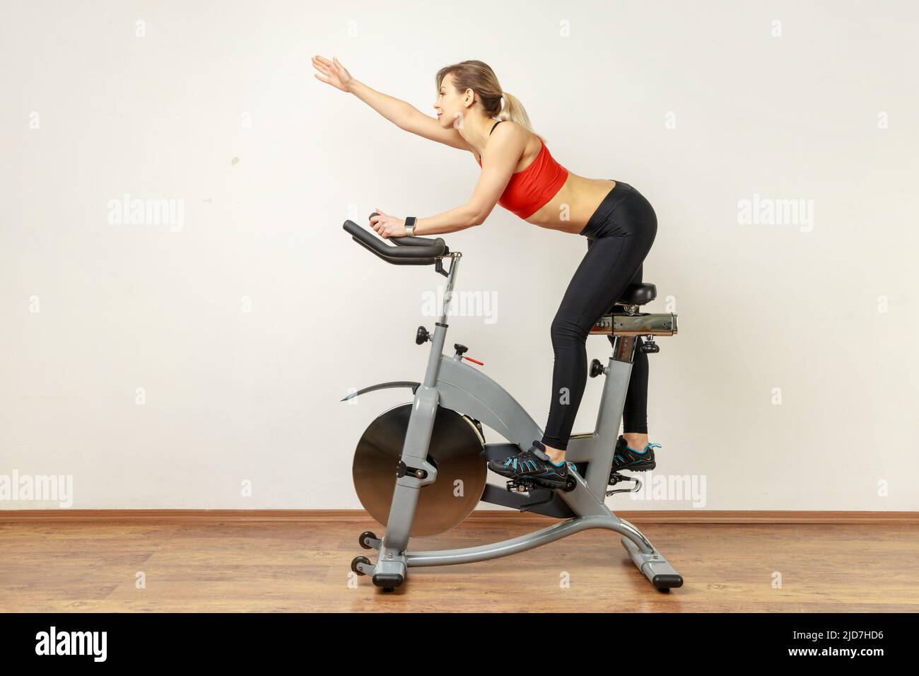 Side view portrait of slim woman riding exercise bike and raised arm ...