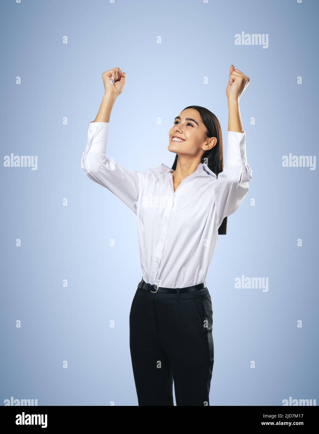 Joyful and satisfied woman in white shirt with raised hands showing her ...