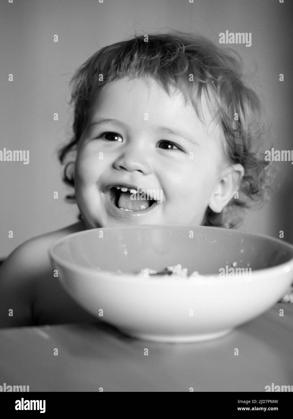 Funny little baby in the kitchen eating with fingers from plate. Fun ...