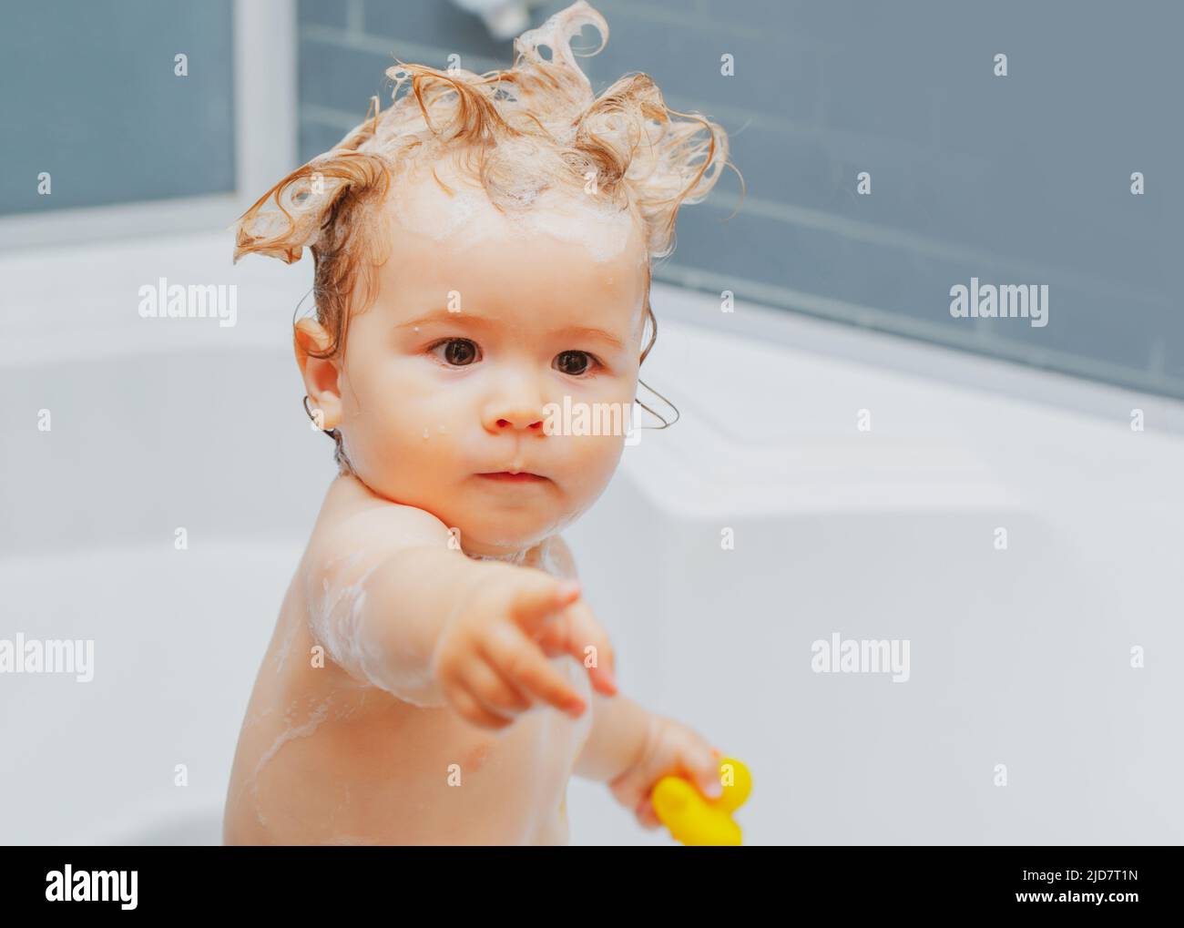 Funny blond kid boy having fun with water by taking bath in bathtub ...