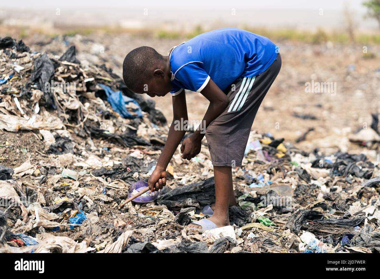 Young black boy poking aroung with a stick in a huge mountain of ...