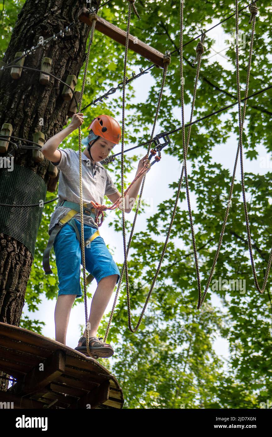 Rope park. A boy teenager in a helmet walks on suspended rope ladders ...