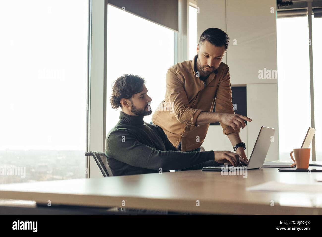 Focused male coworkers communicating, using laptop pc at desk in ...