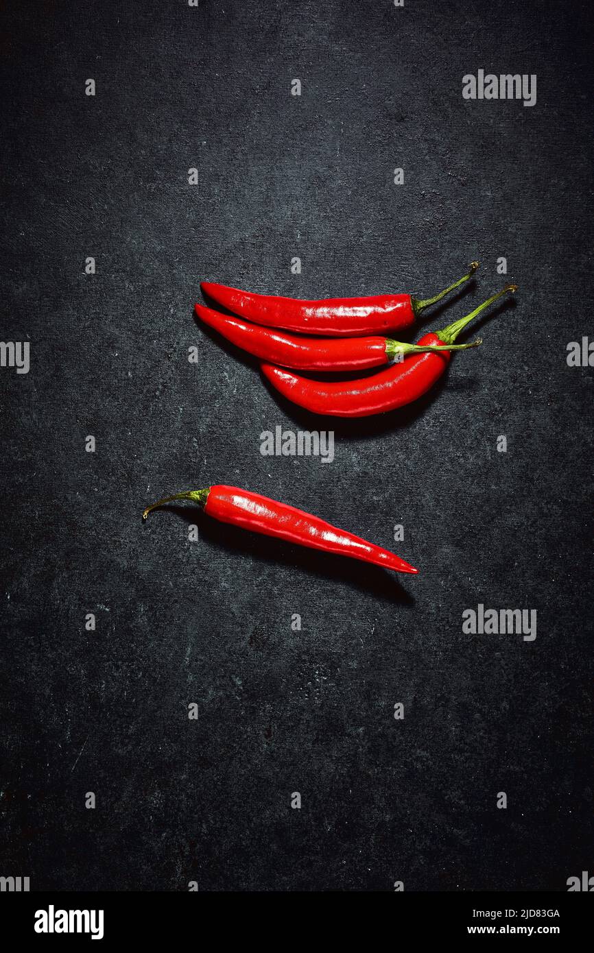 Red chilli peppers over dark background. Top down shot of glossy ...