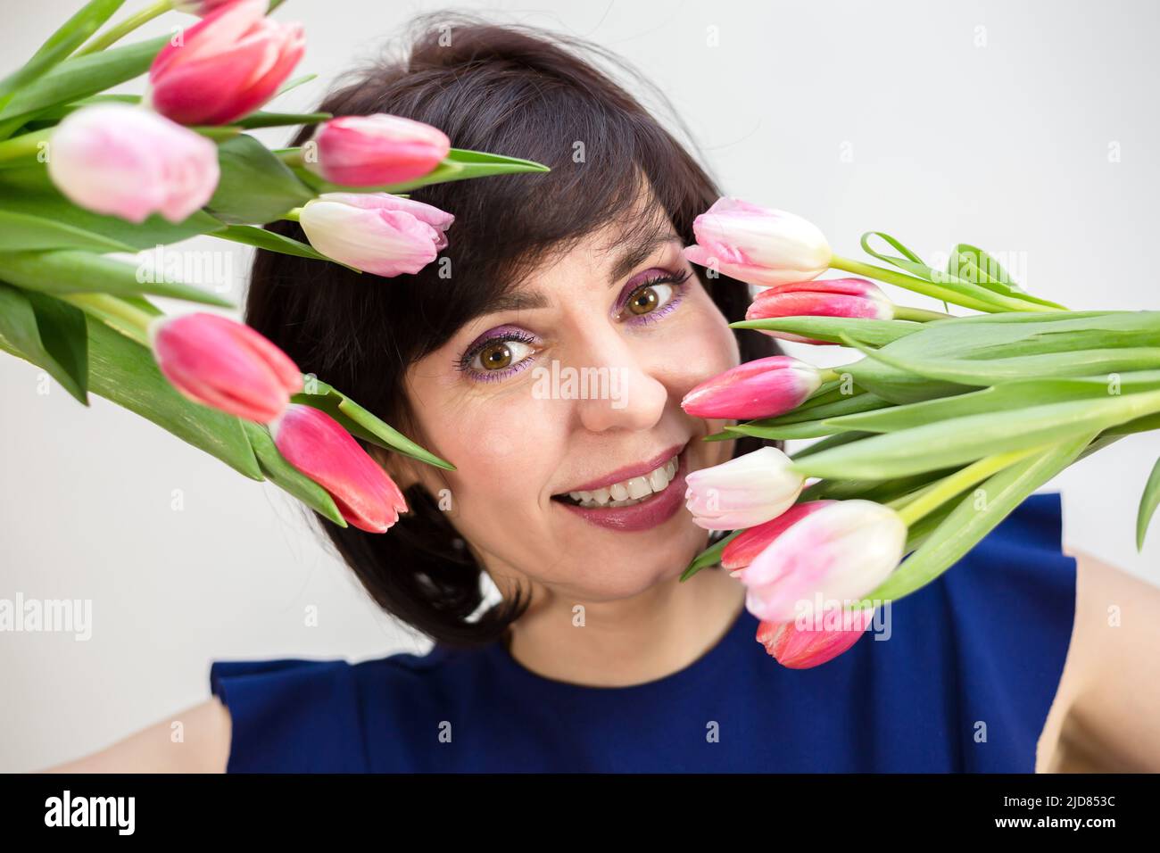 Portrait of an adult brunette covering her face with two bouquets of ...