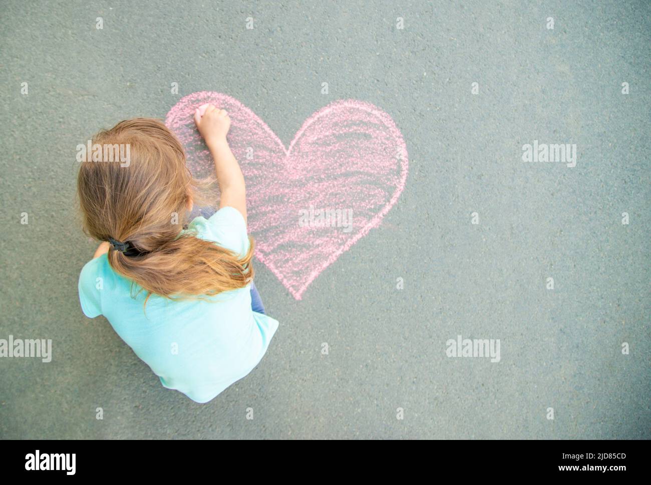 the child paints chalk on the asphalt heart. Selective focus Stock ...