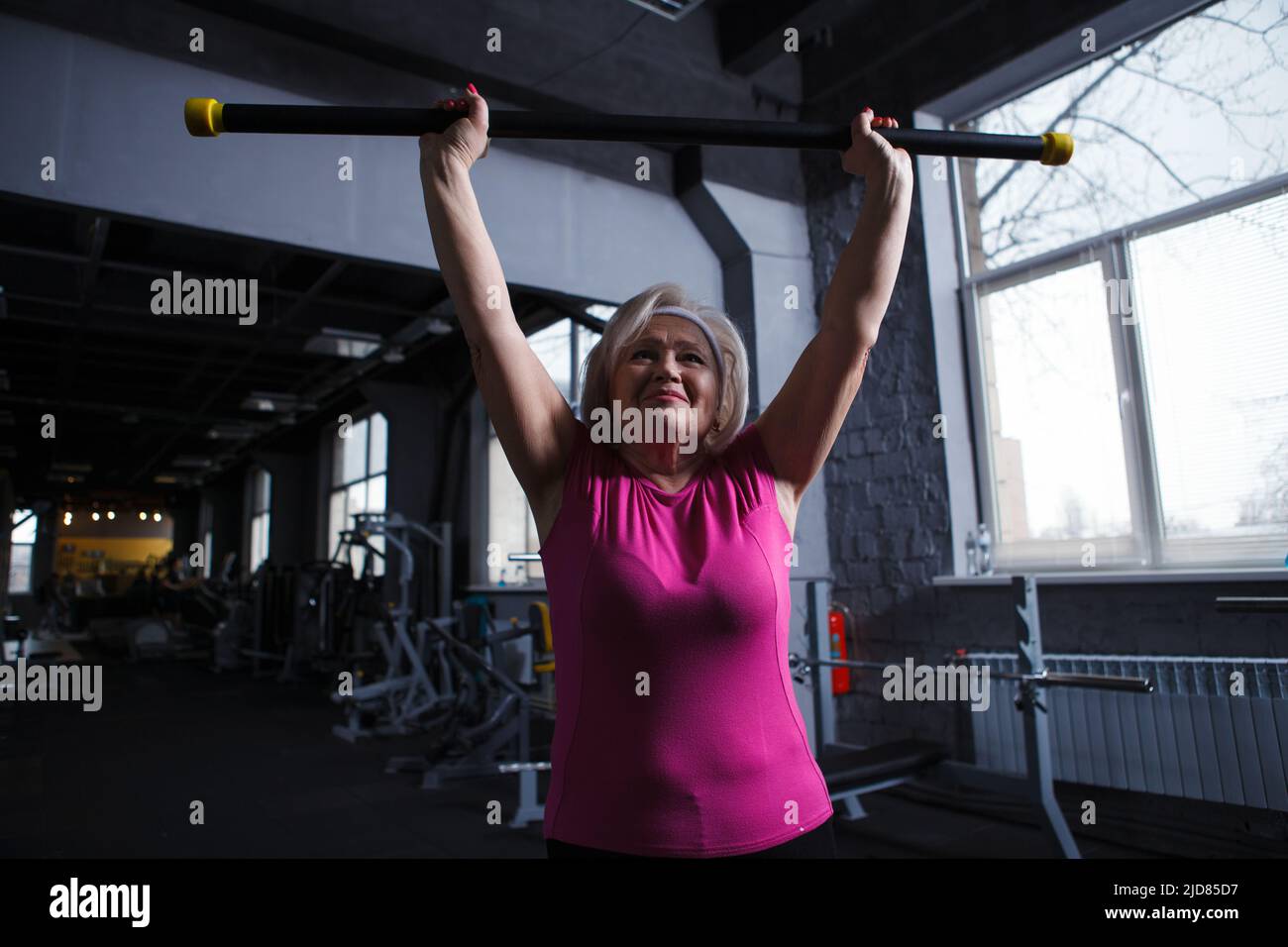 Strong healthy elderly woman lifting barbell, doing chest press Stock ...