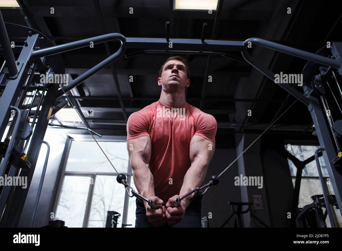 Low angle shot of a muscular athlete exercising in cable crossover gym ...
